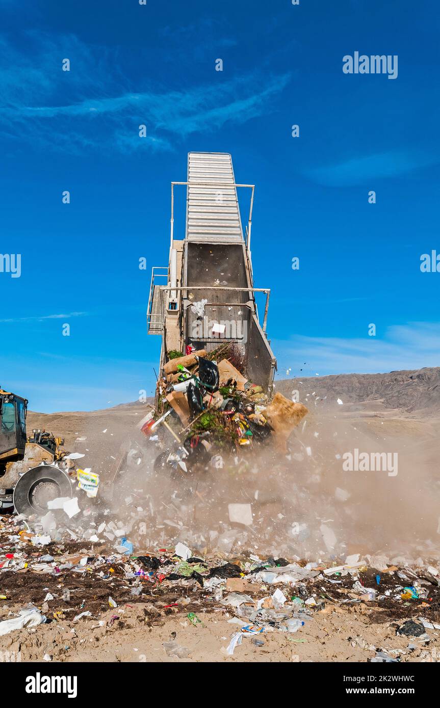 A trailer from a semitrailer truck is in a landfill tipper being raised ...