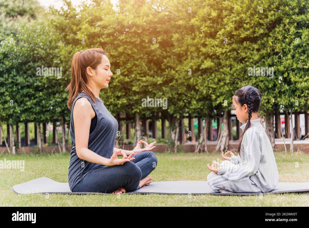 mother practicing doing yoga exercises with her daughter outdoors in meditate pose together ...