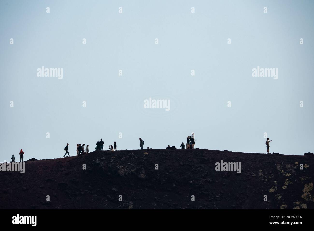 Tourists hiking through volcanic Mount Etna with smoky sky in ...