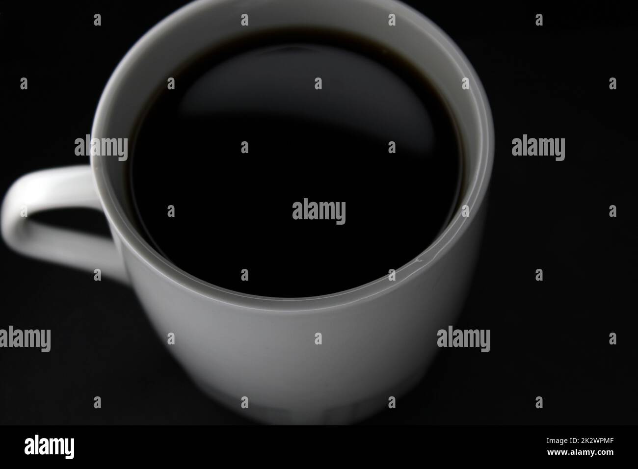 White mug with black coffee on a black background. View from above ...