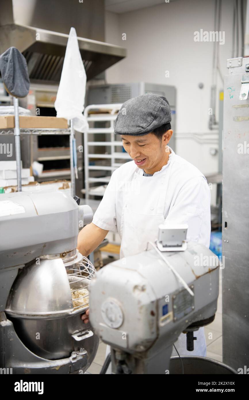 Male baker preparing dough in commercial mixer in bakery kitchen Stock ...