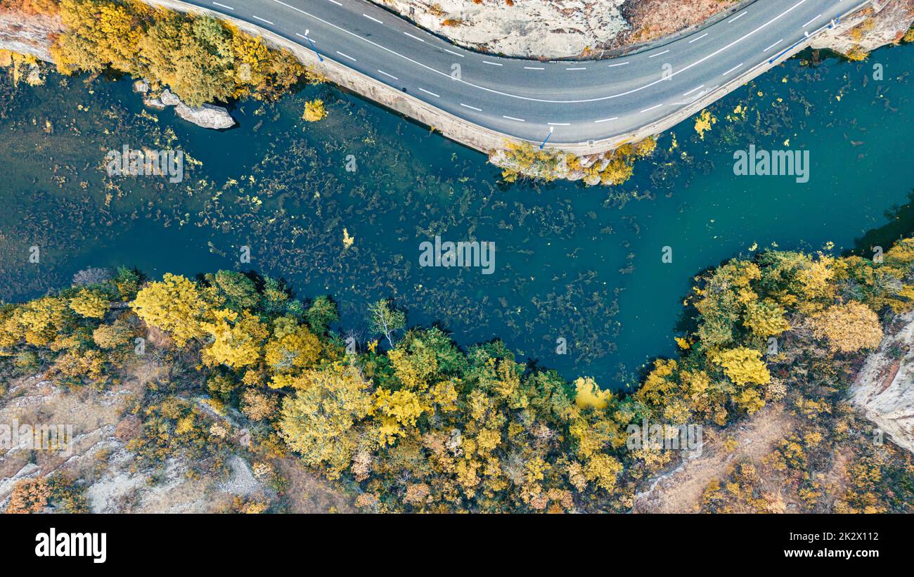 A road on a mountain slope overlooking a river with colorful vegetation ...