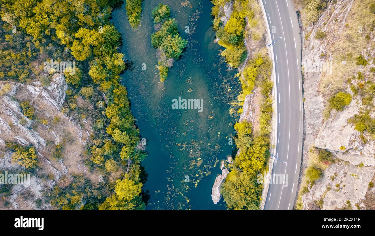 A road on a mountain slope overlooking a river with colorful vegetation ...
