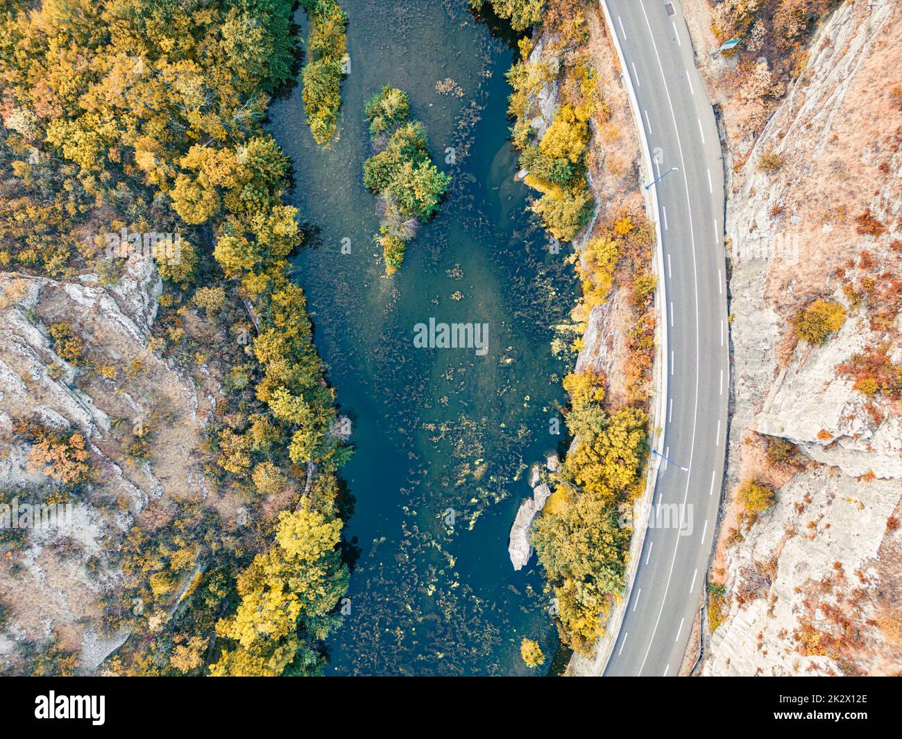 A road on a mountain slope overlooking a river with colorful vegetation ...