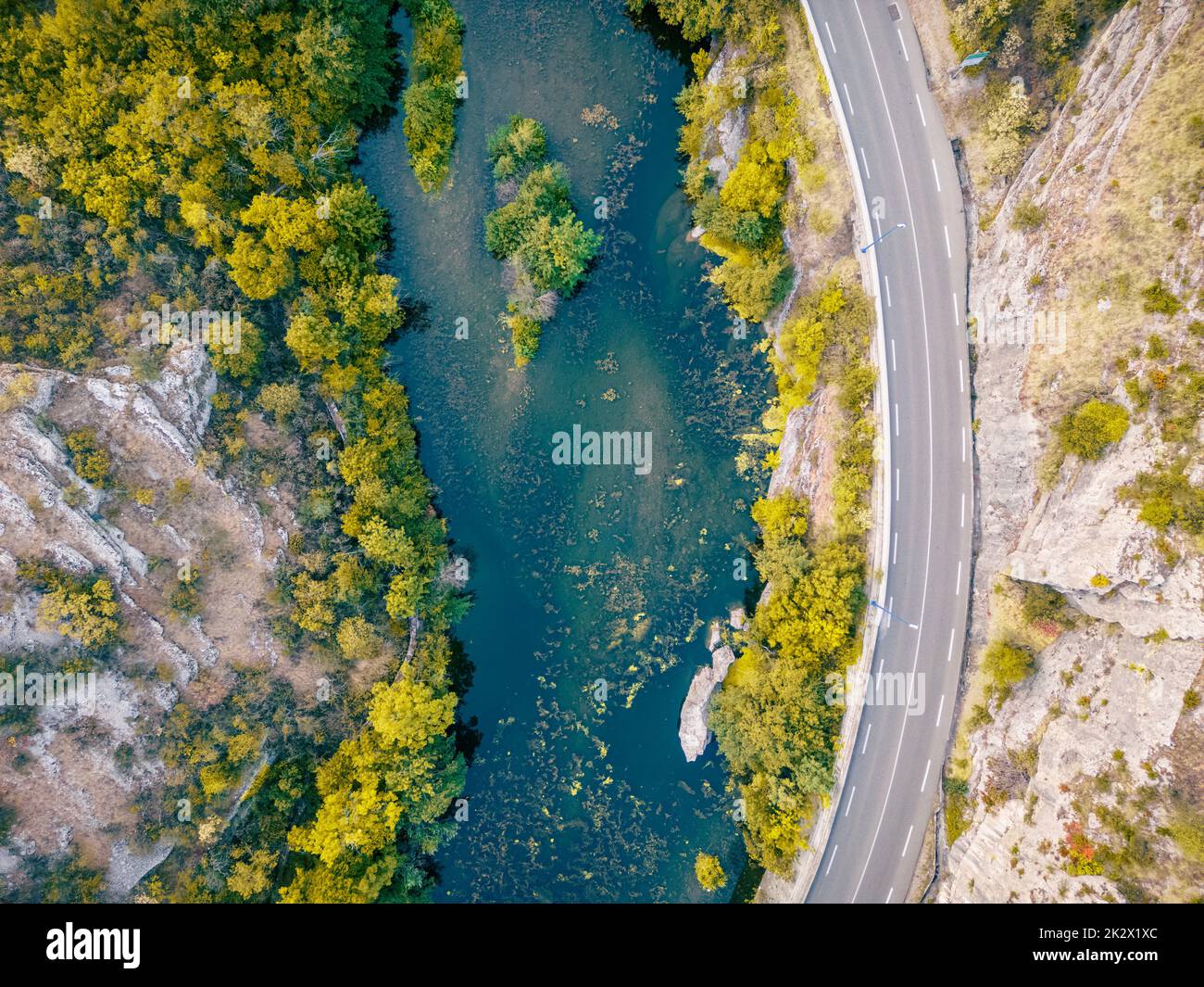 A road on a mountain slope overlooking a river with colorful vegetation ...