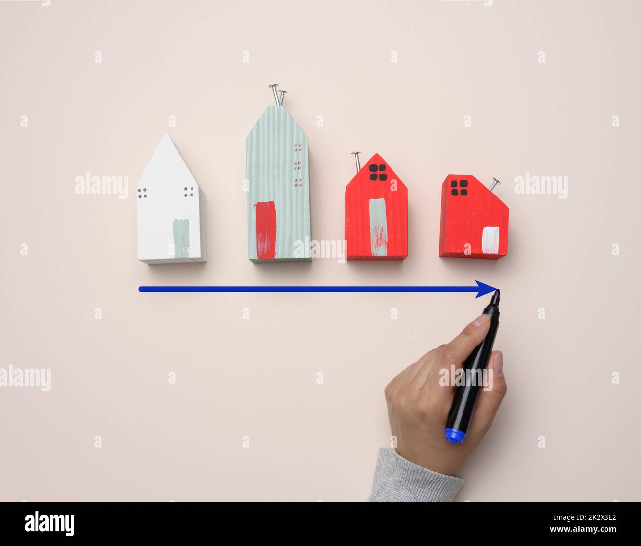 A miniature wooden house and a woman's hand draws a graph with growing ...