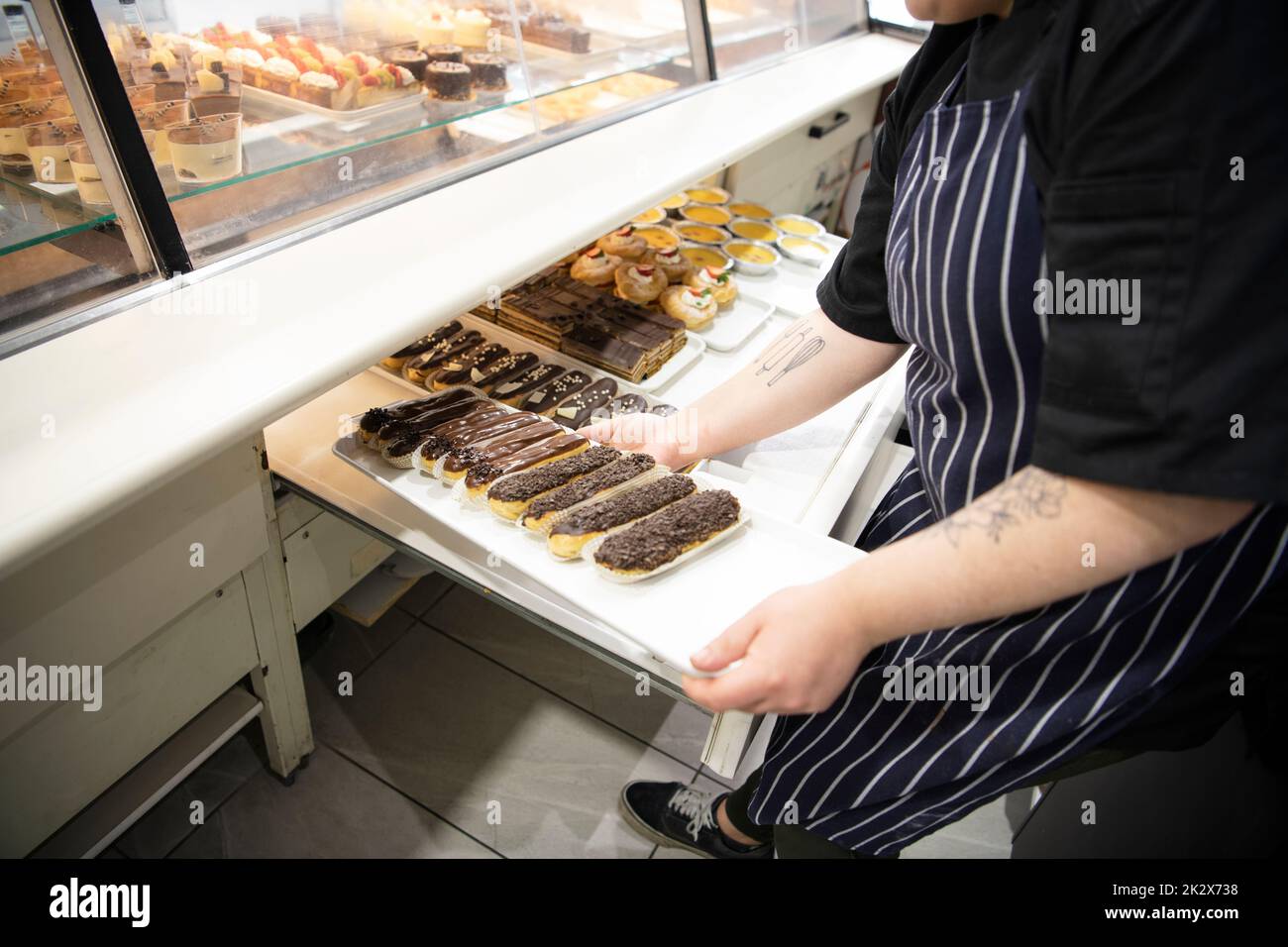 Female pastry shop owner placing chocolate French eclairs in display ...