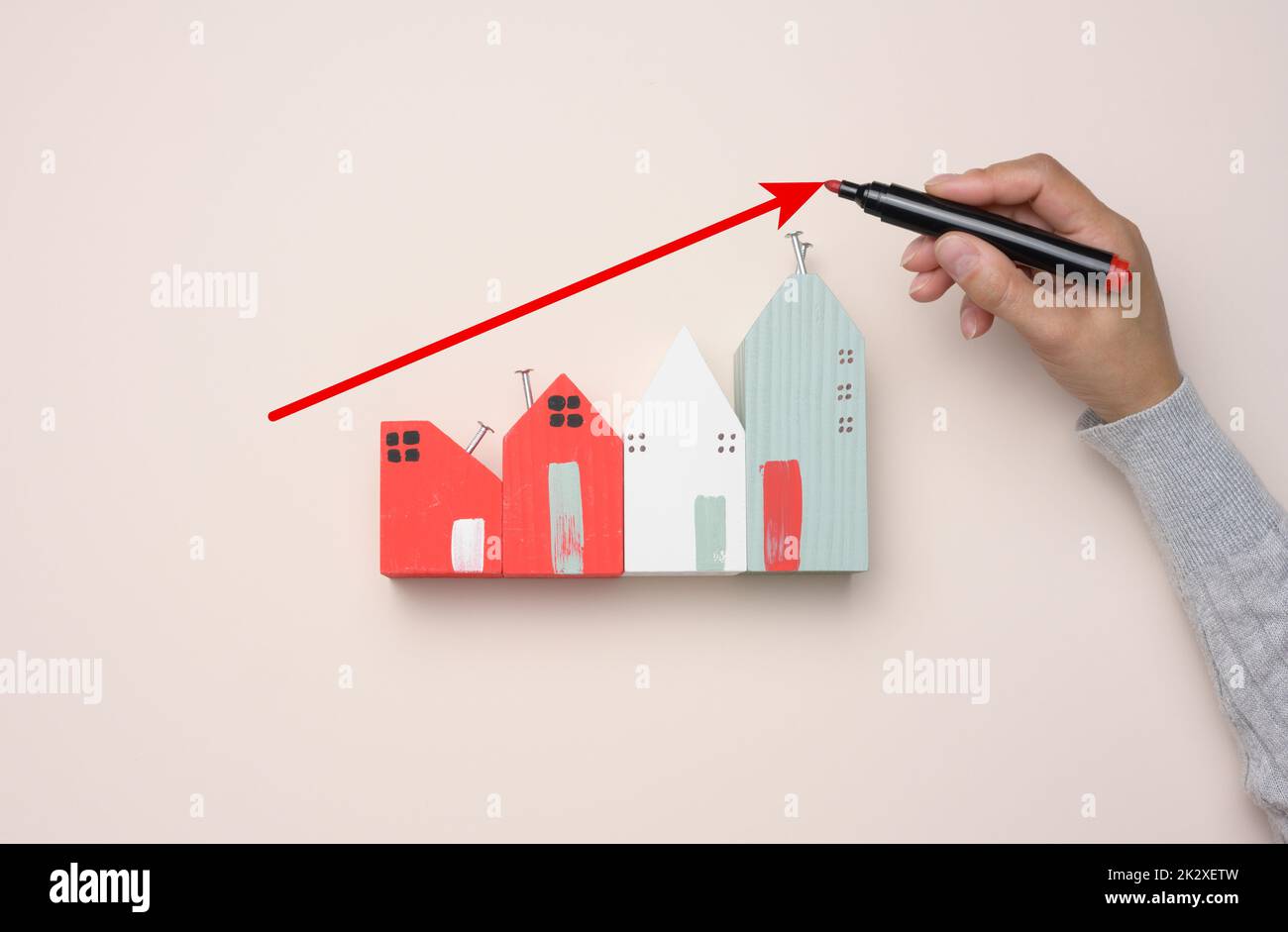 A miniature wooden house and a woman's hand draws a graph with growing ...