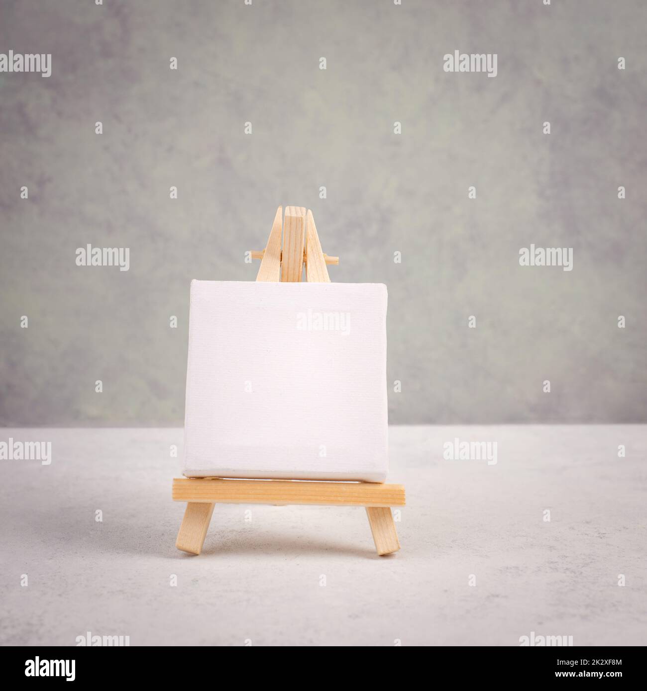 Easel with blank white canvas in front of a gray textured background ...
