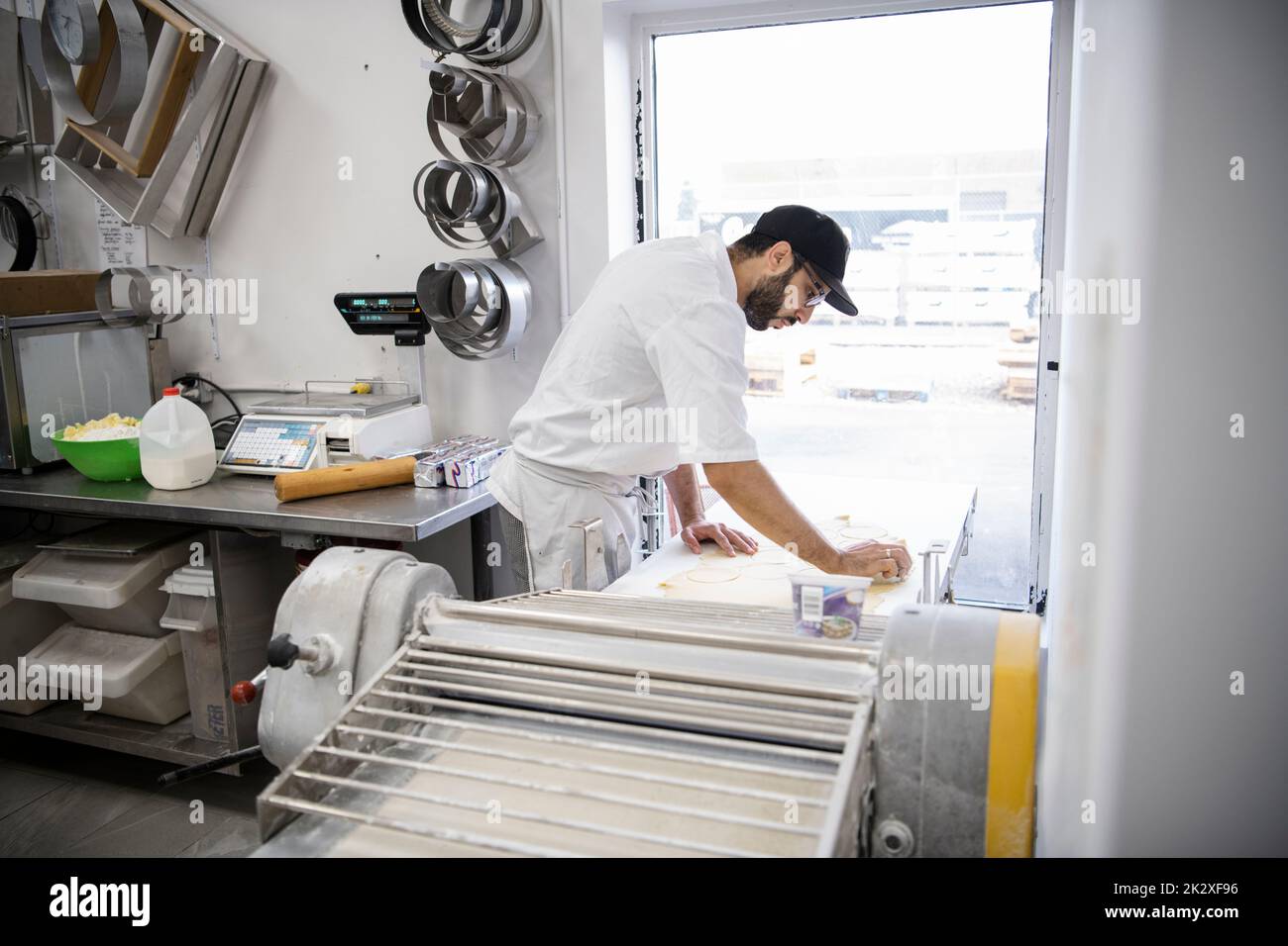 Male baker cutting pastry dough at dough sheeter in bakery kitchen ...