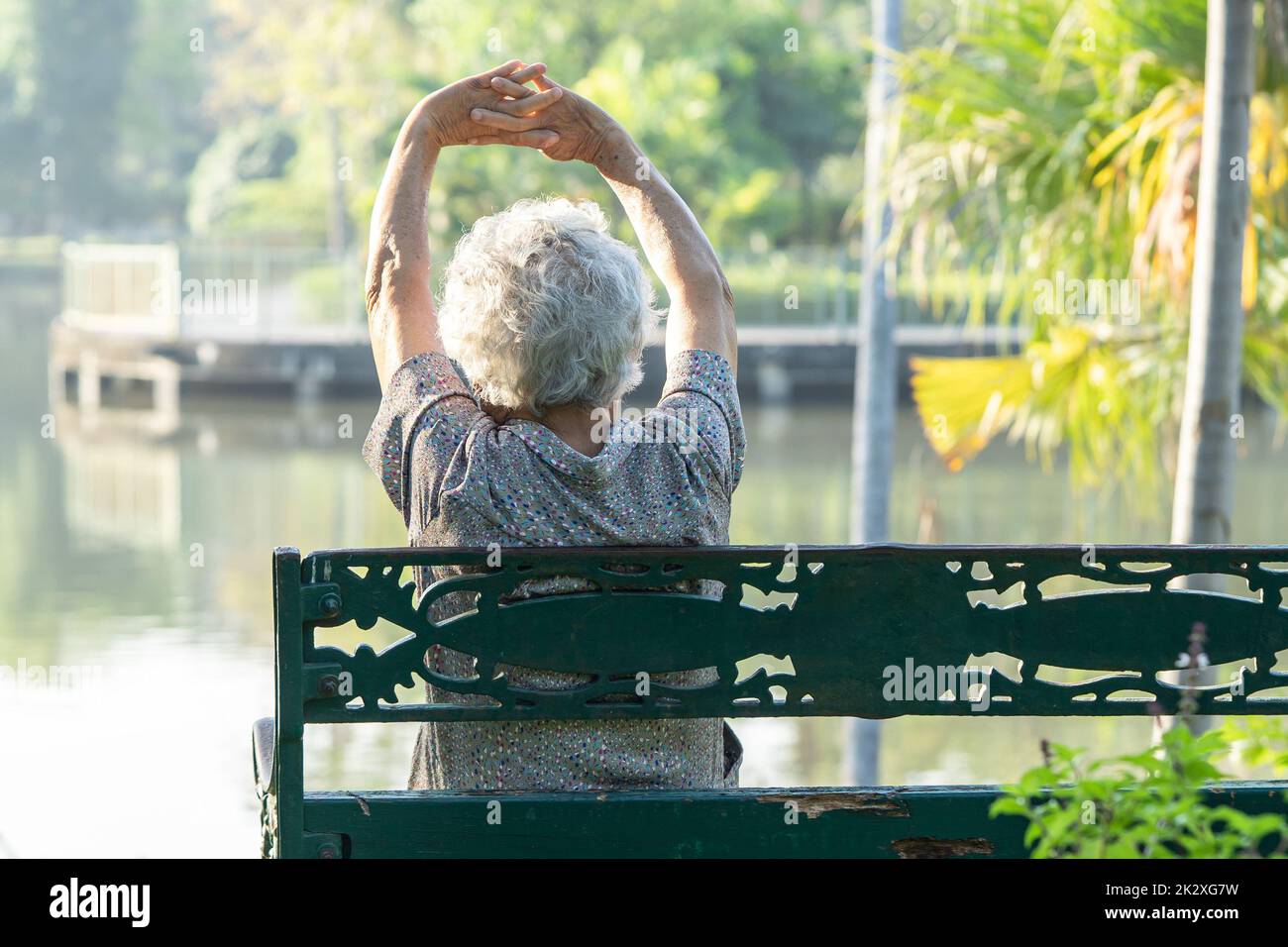 Asian elderly woman happy and fresh sitting back on bench in autumn ...