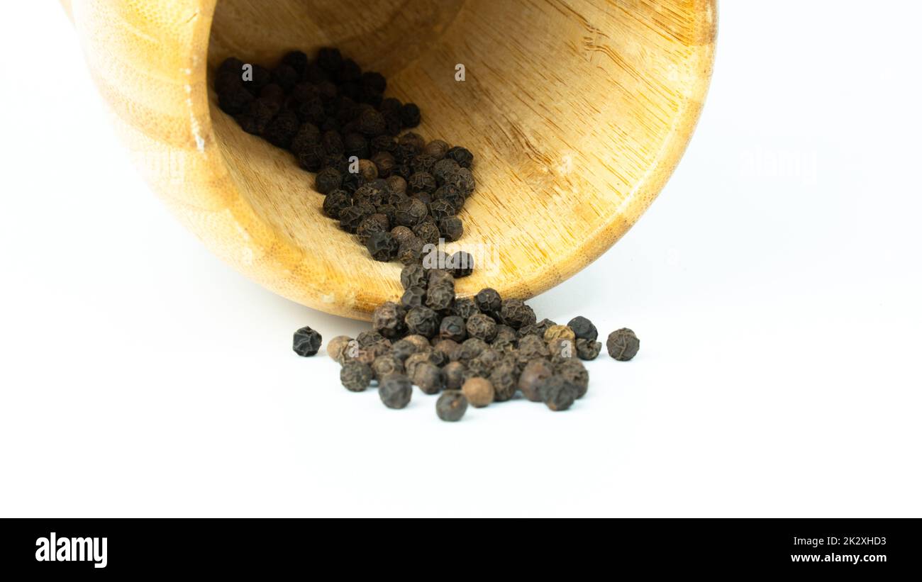 Black pepper pouring from the wooden bowl isolated on white background ...
