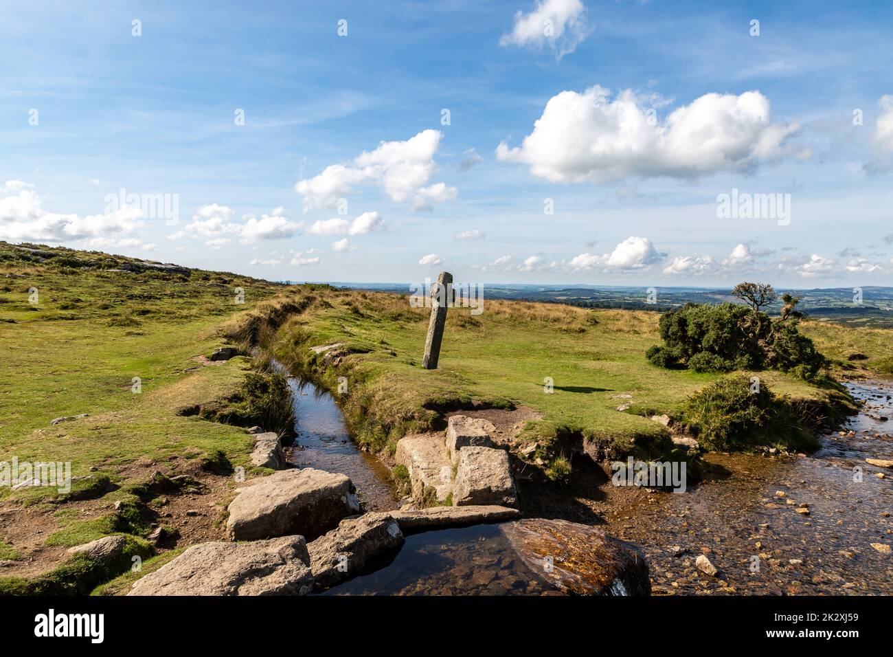 A stream in Dartmoor National Park with Windy Post Granite Cross behind ...