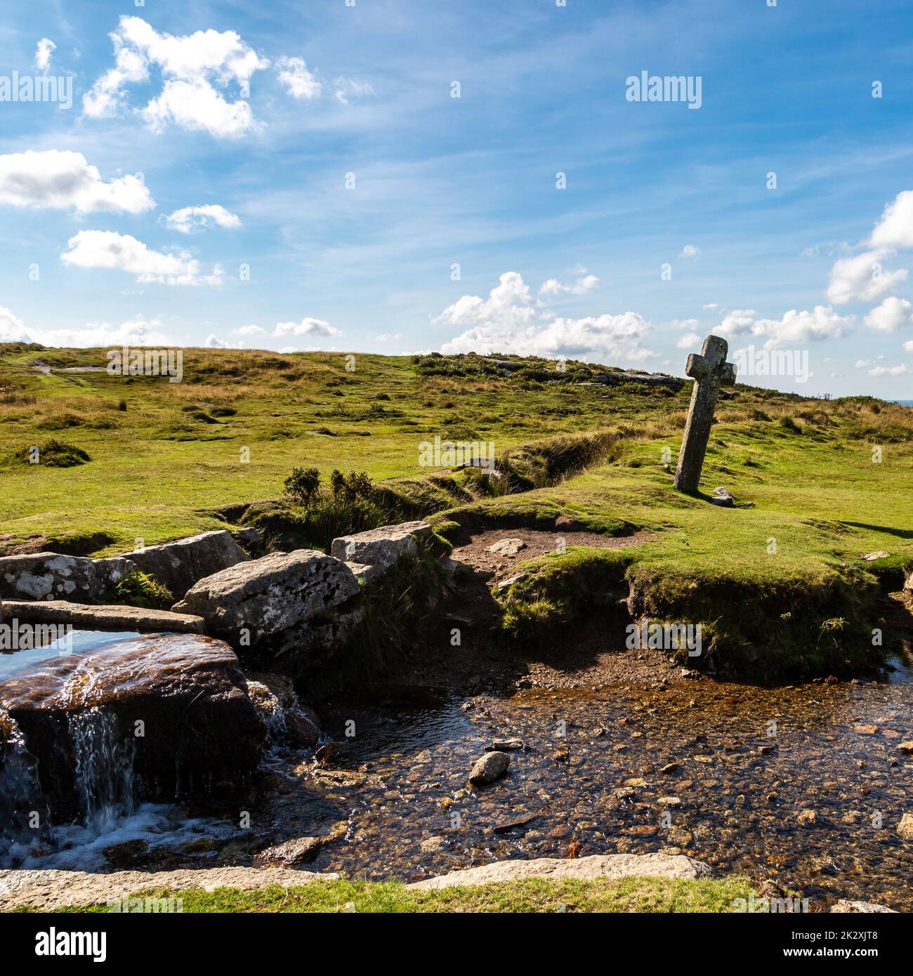 A stream in Dartmoor National Park with Windy Post Granite Cross behind ...