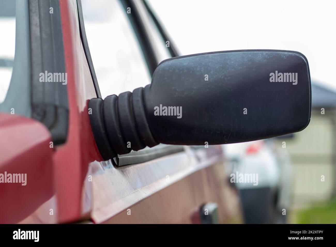 Side left black plastic rearview mirror on a red car. Exterior side ...