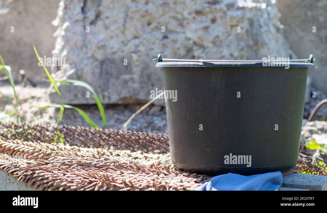 Black plastic bucket with water in the summer garden. Rainwater tank in ...