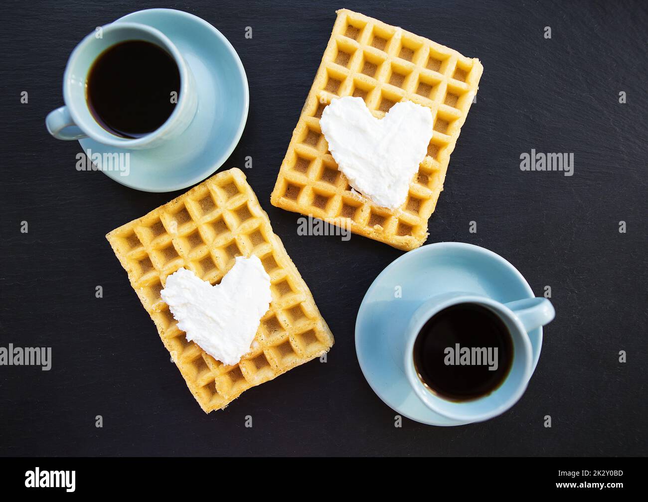 Delicious Belgian waffles with cream on a black background and two cups ...