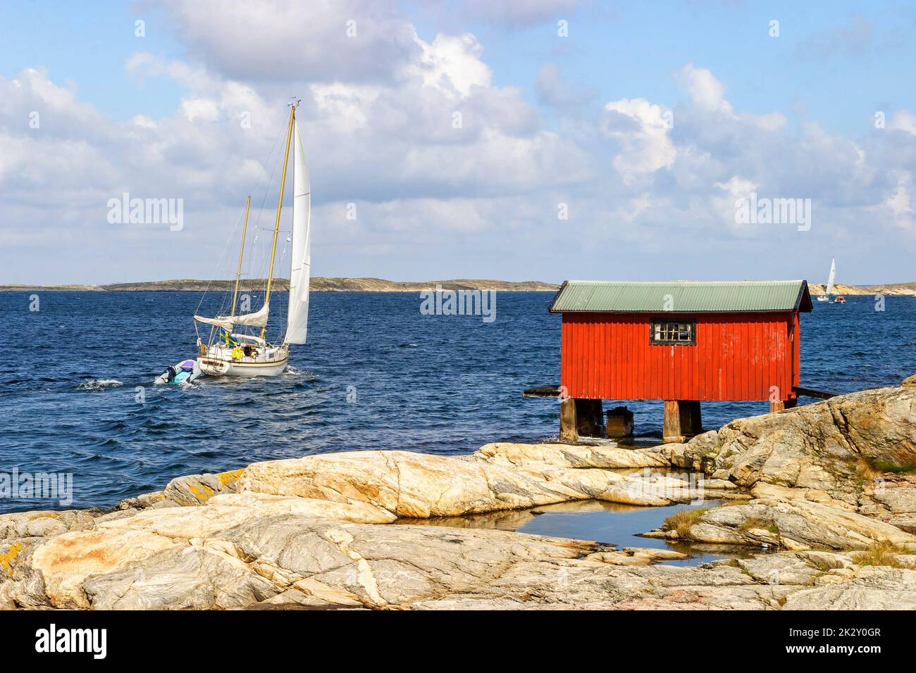 Sailboat at sea with a red boathouse on the rocks in the archipelago ...