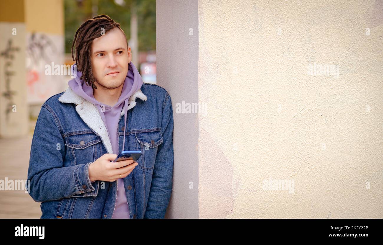 Portrait of young handsome man with dreadlocks browsing mobile phone ...