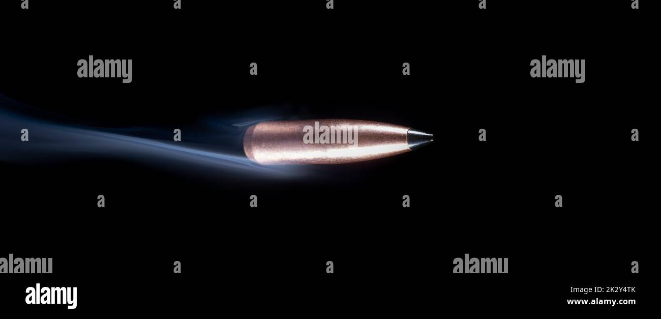 Copper plated bullet on a dark background flying with smoke behind ...