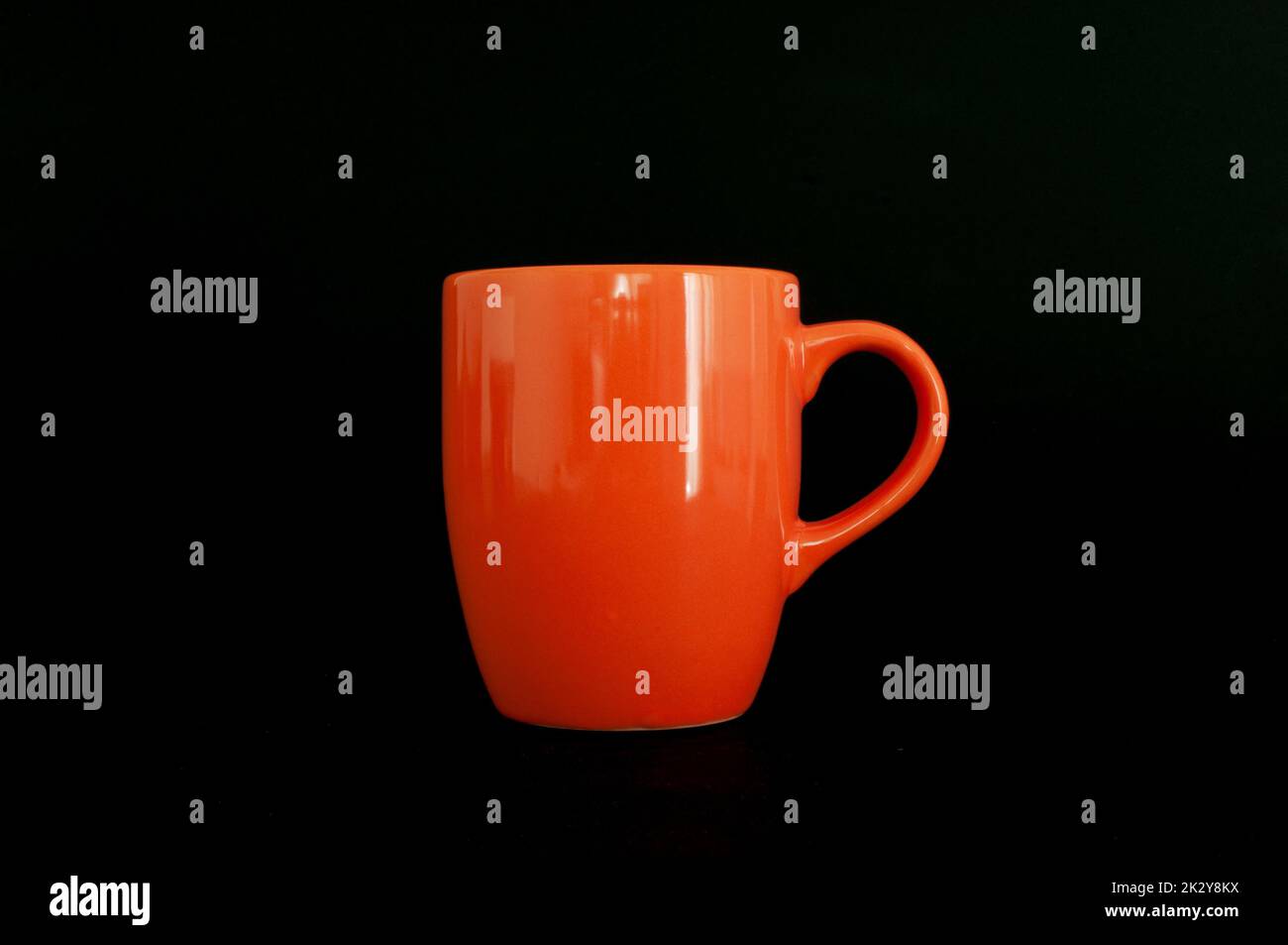 Profile view of orange color tea mug or cup isolated on dark background ...