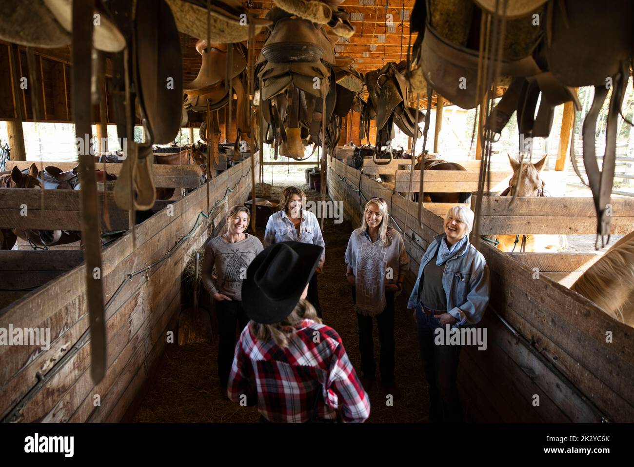 Women friends listening to horseback riding guide in horse barn Stock ...