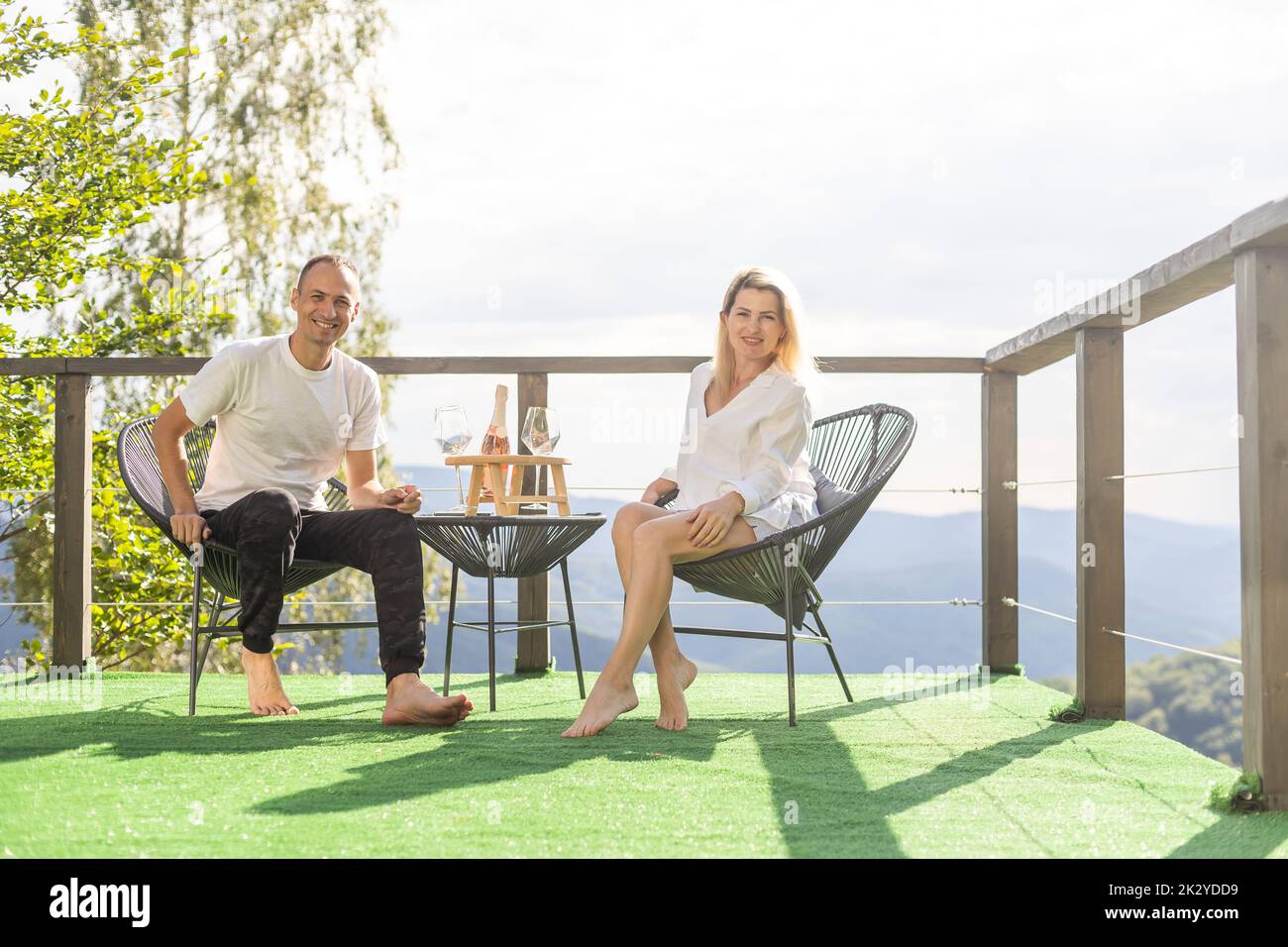 Happy couple sit on wicker chairs at outdoor terrace in the mountains ...