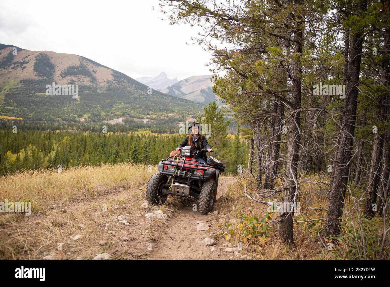 Happy female rancher riding quad bike on rugged mountain trail in woods ...