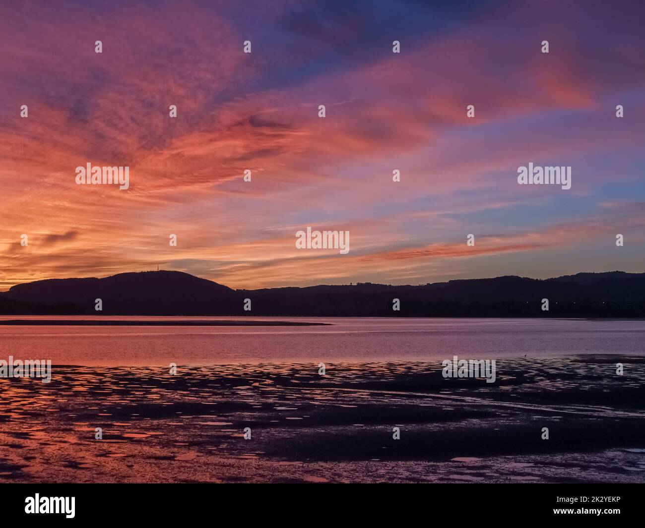Dramatic deep colours of brilliant sunrise over bay in Tauranga Harbour ...