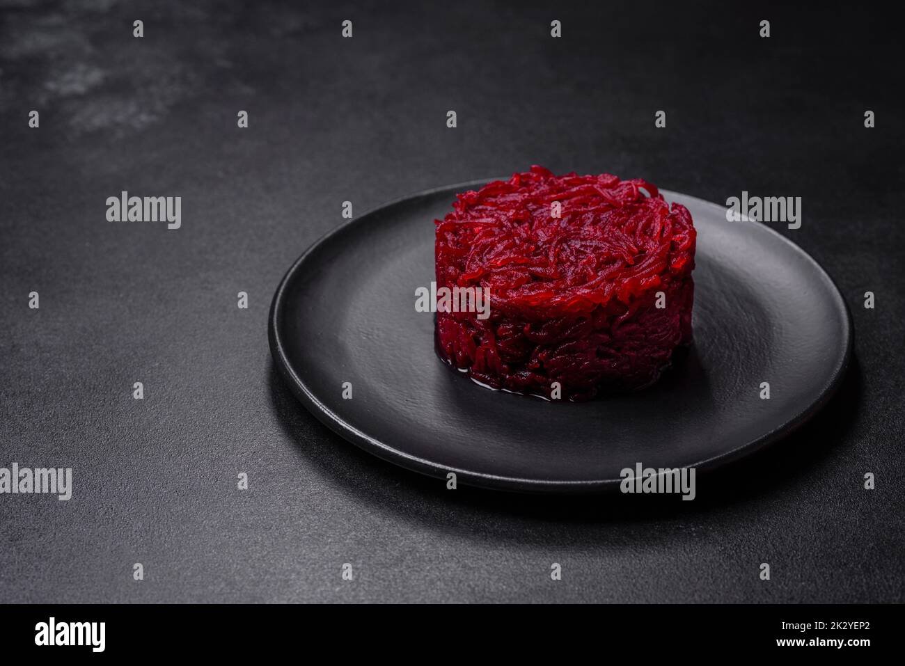 Cooked grated beetroot formed as a cylinder and ready dish on a black ...
