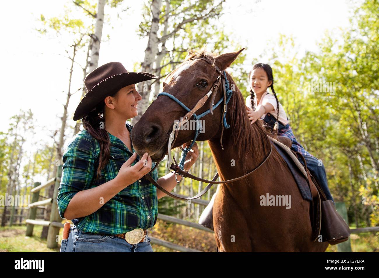 Happy female rancher helping girl horseback riding on autumn ranch ...