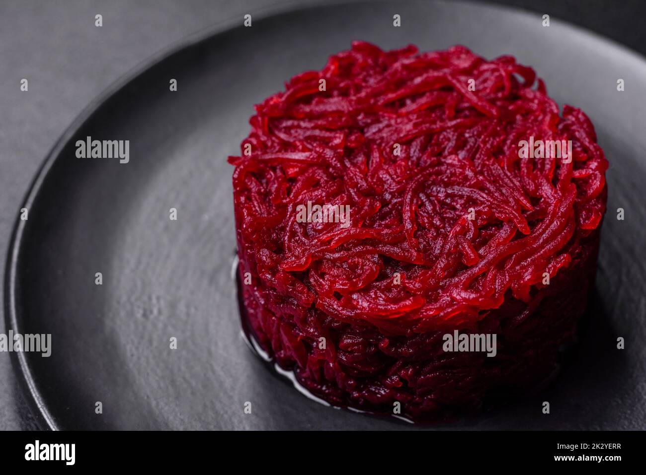 Cooked grated beetroot formed as a cylinder and ready dish on a black ...
