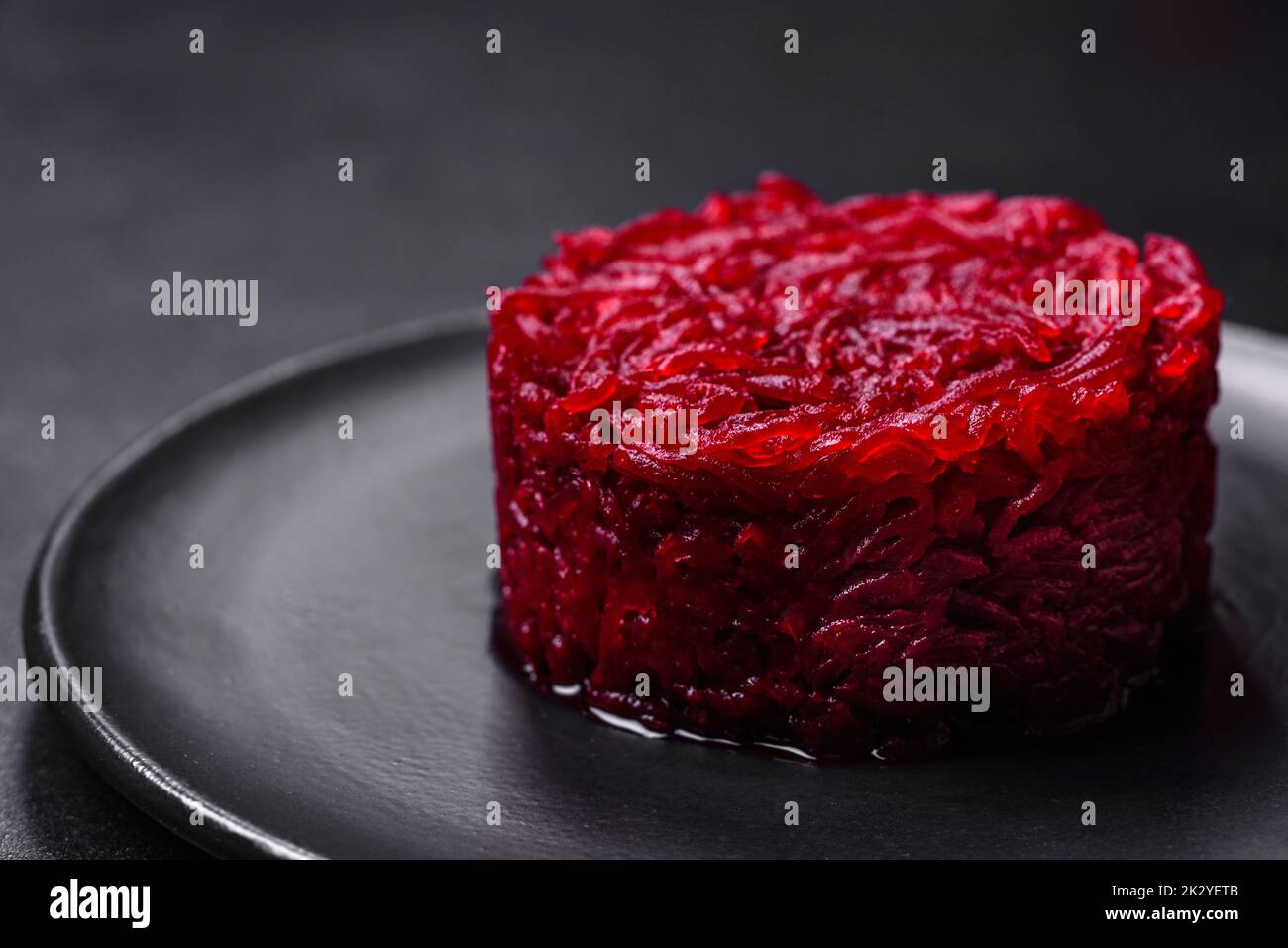 Cooked grated beetroot formed as a cylinder and ready dish on a black ...