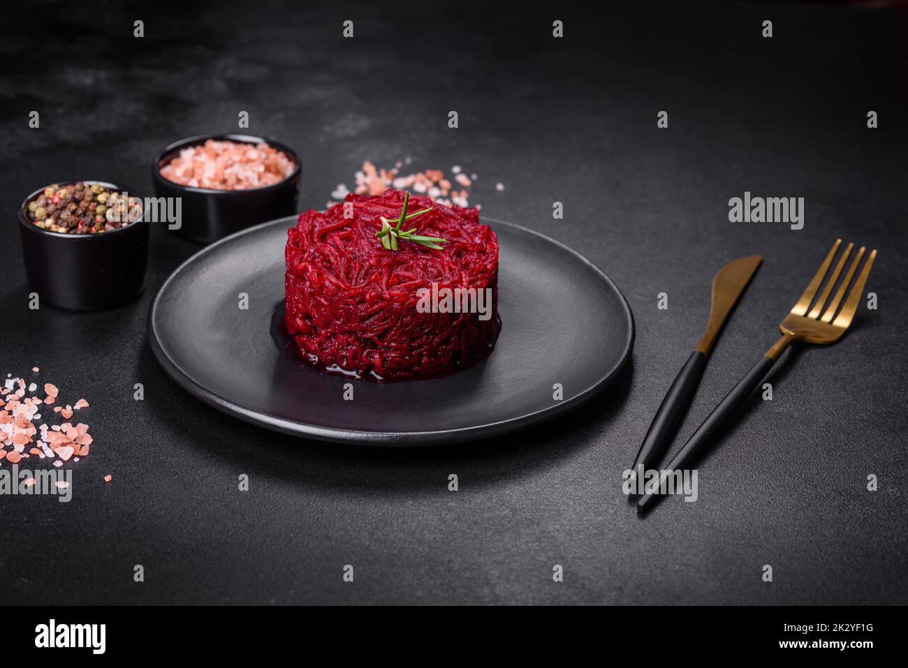 Cooked grated beetroot formed as a cylinder and ready dish on a black ...