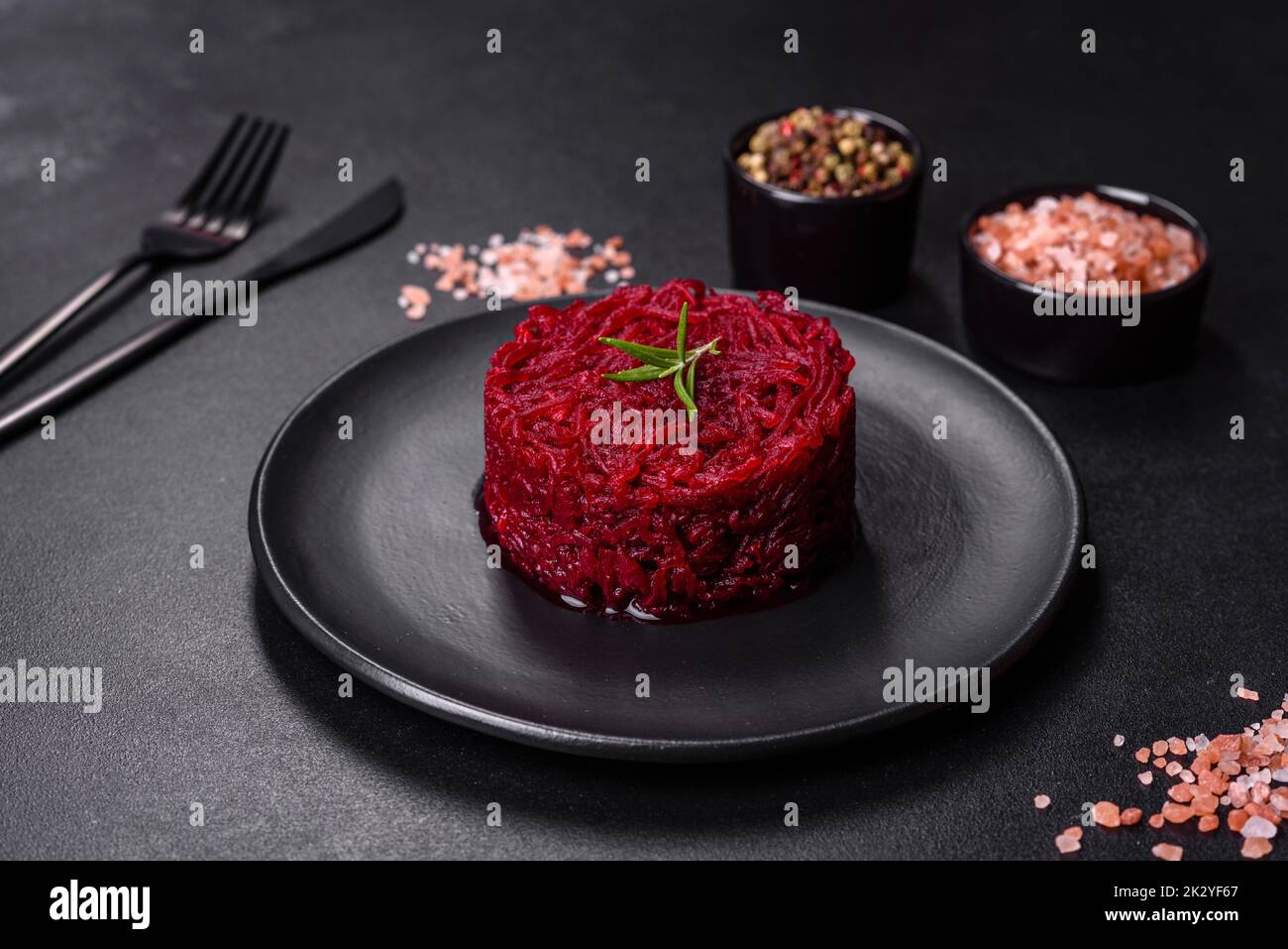 Cooked grated beetroot formed as a cylinder and ready dish on a black ...