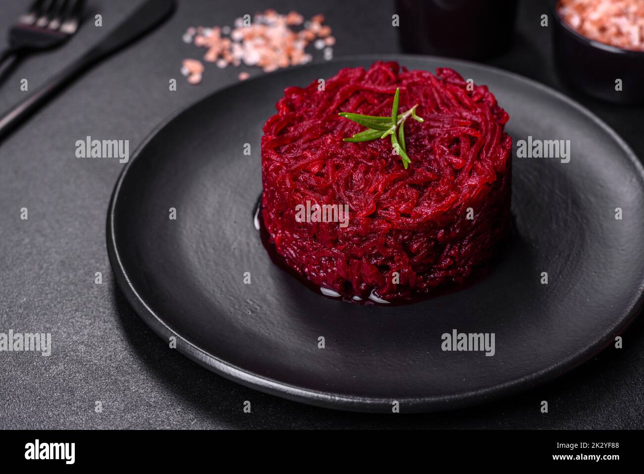 Cooked grated beetroot formed as a cylinder and ready dish on a black ...
