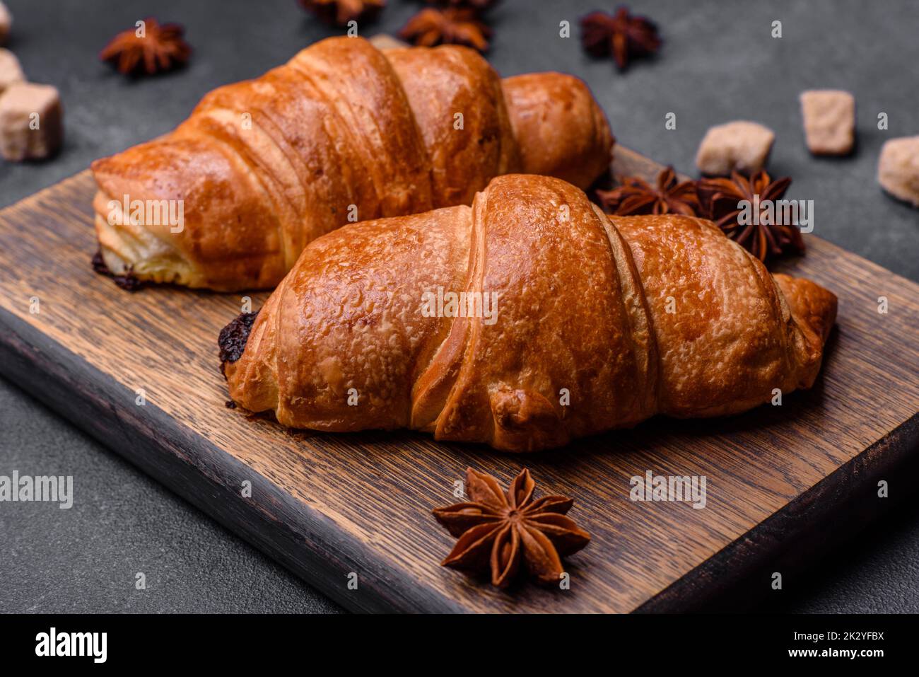 Fresh crisp chocolate croissants on wooden cutting board against dark ...