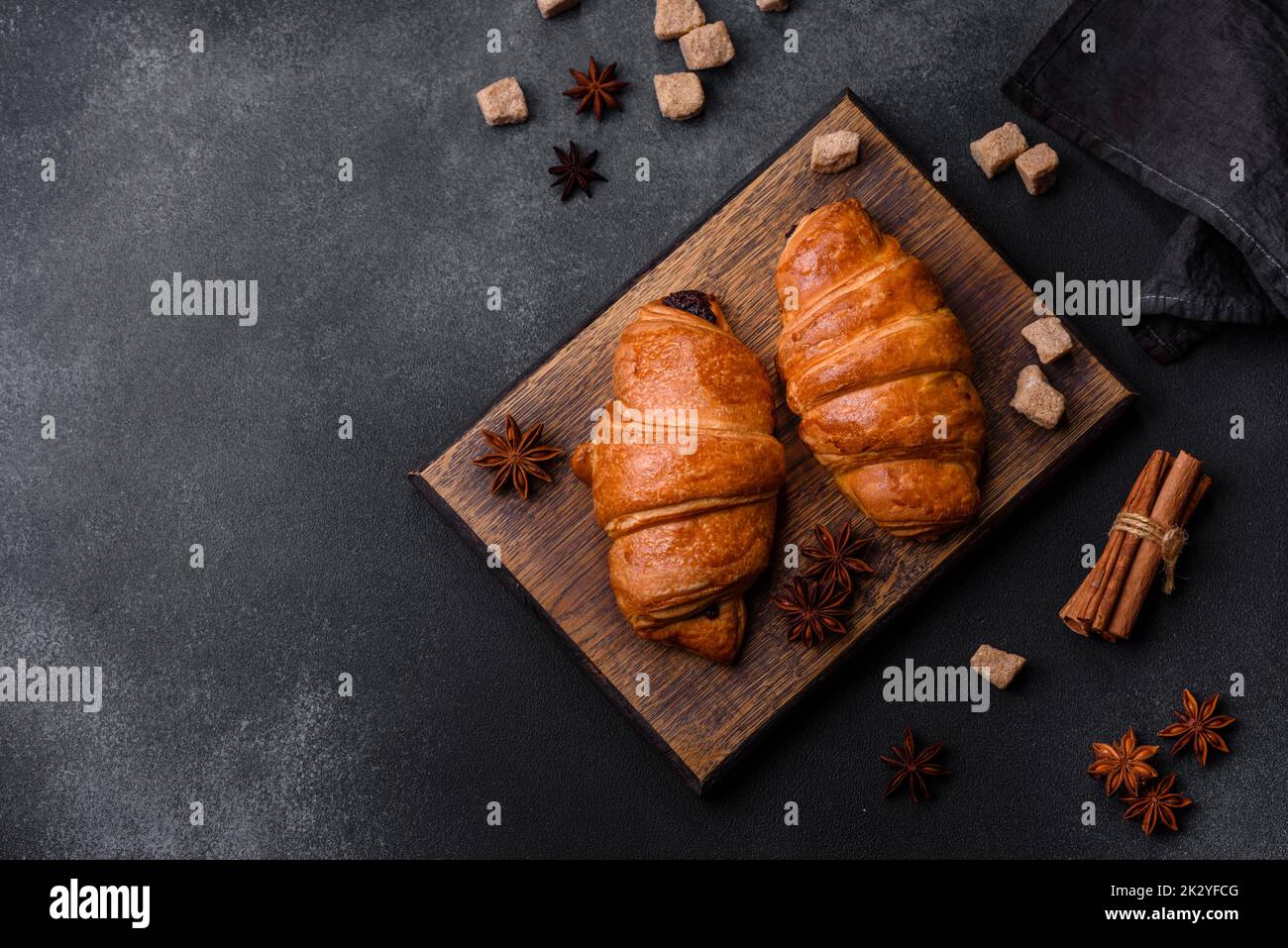 Fresh crisp chocolate croissants on wooden cutting board against dark ...