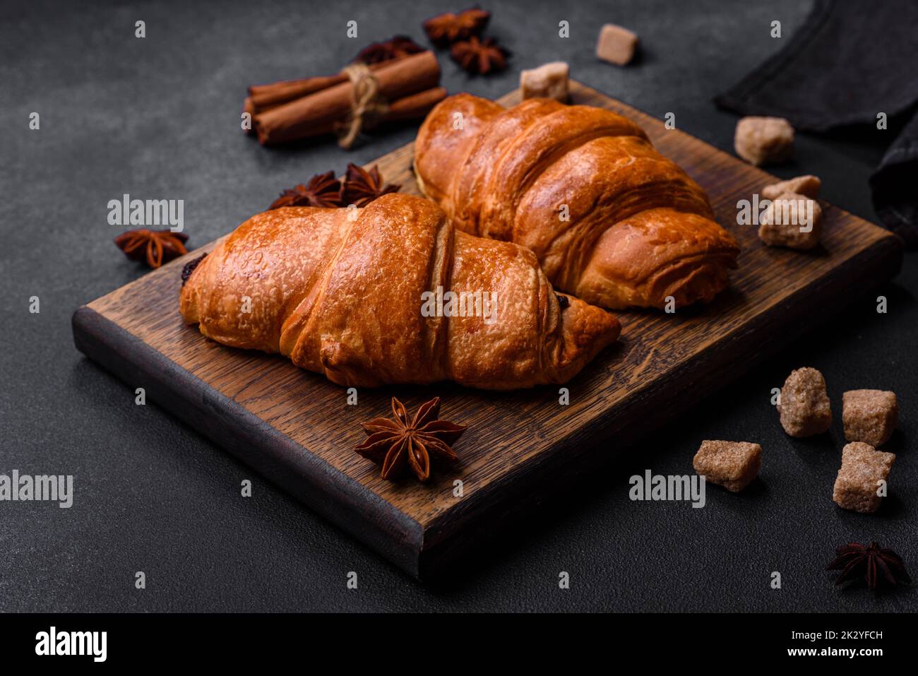 Fresh crisp chocolate croissants on wooden cutting board against dark ...