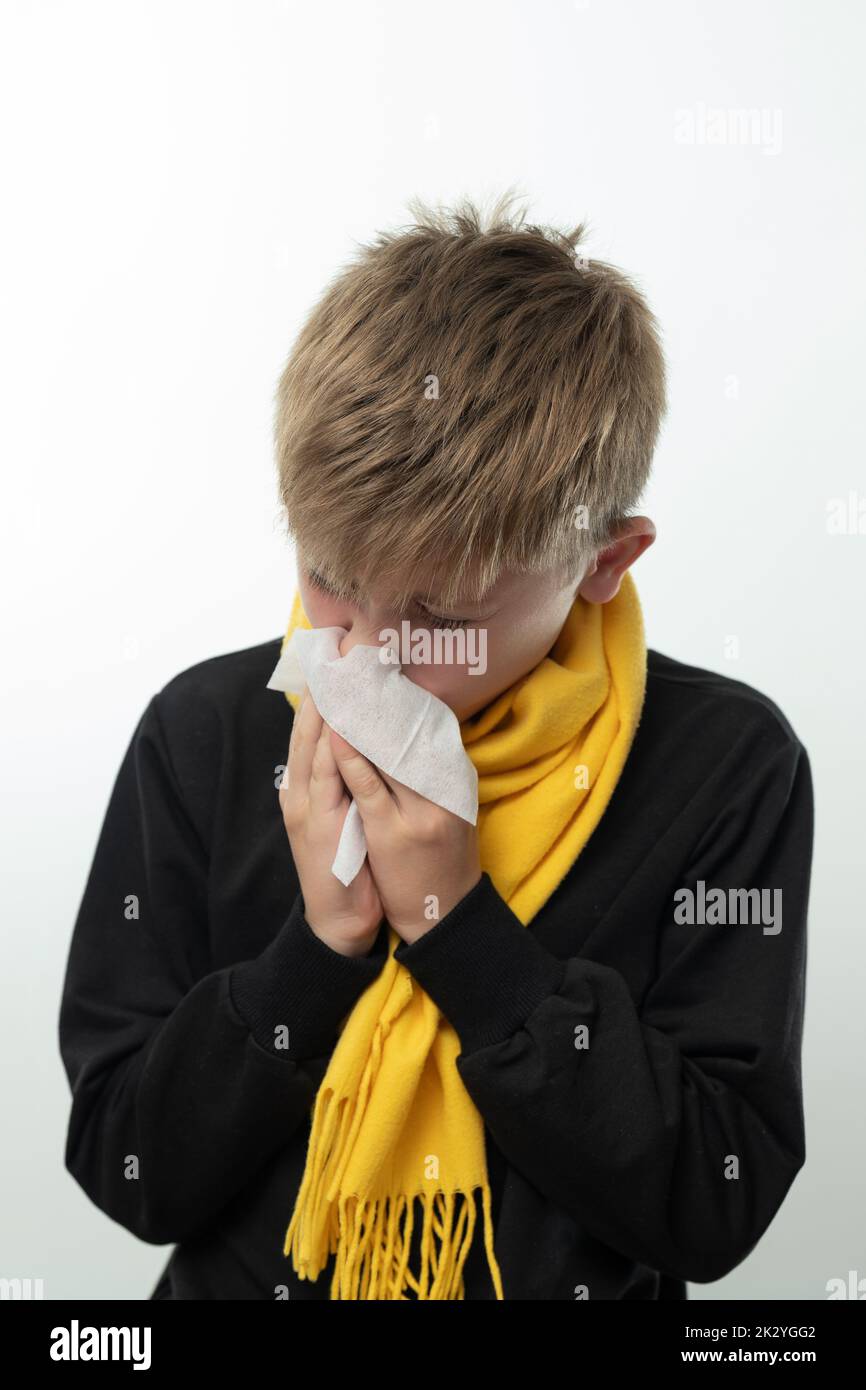 The boy wrapped in a scarf has a runny nose and blows his nose into a ...