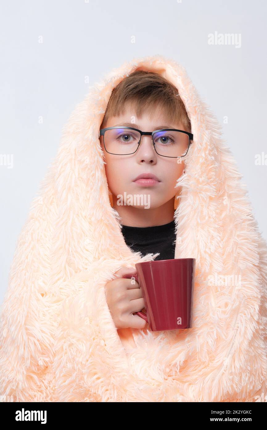 A boy with the flu is wrapped in a blanket and drinks hot tea, the ...