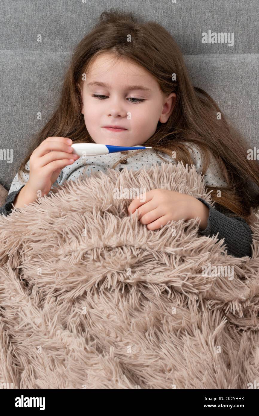 A cute little girl is lying in bed sick, the child measures the ...