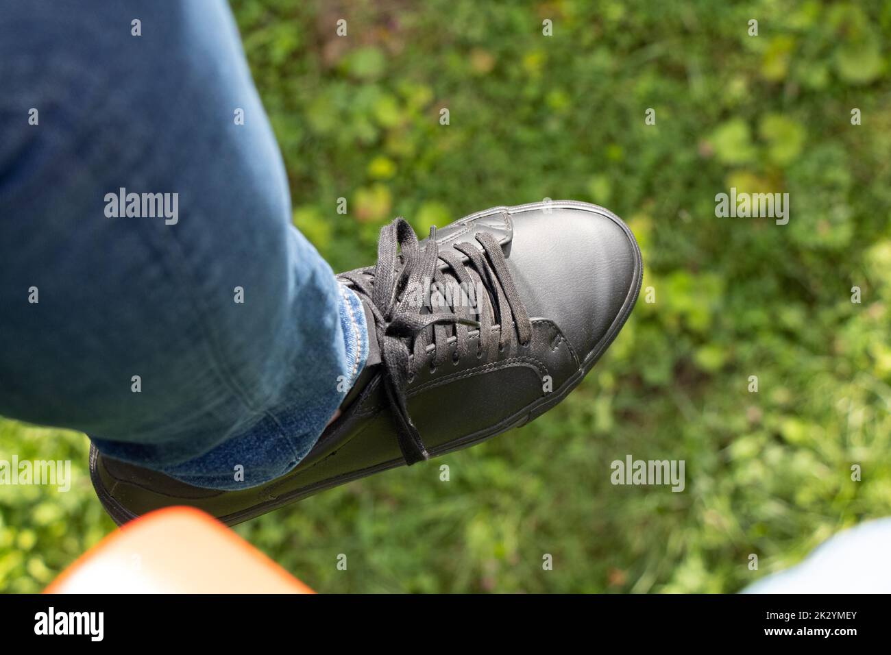 Men's legs in black sneakers and jeans on a green background of grass ...