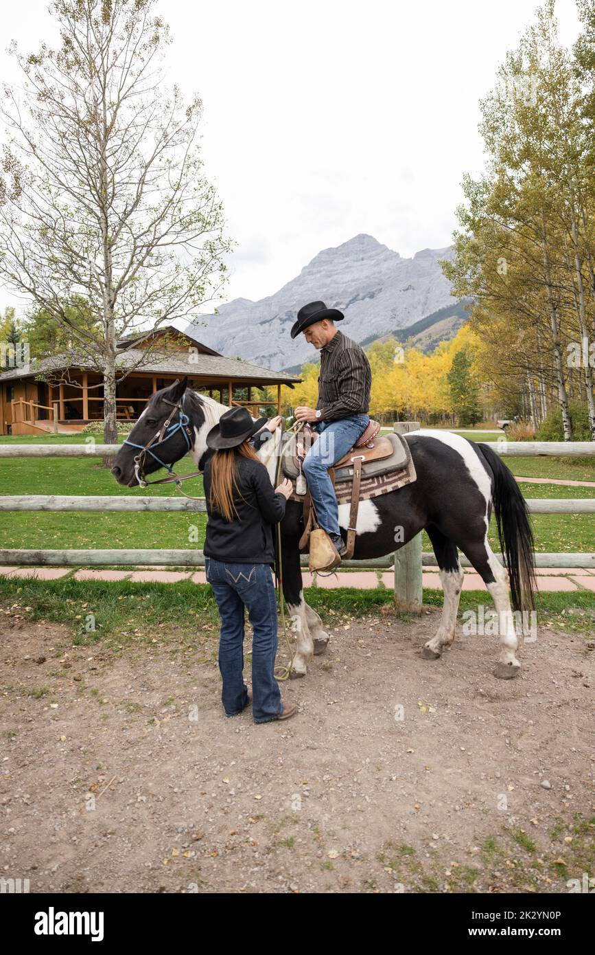 Female rancher helping man prepare for horseback riding on ranch Stock ...