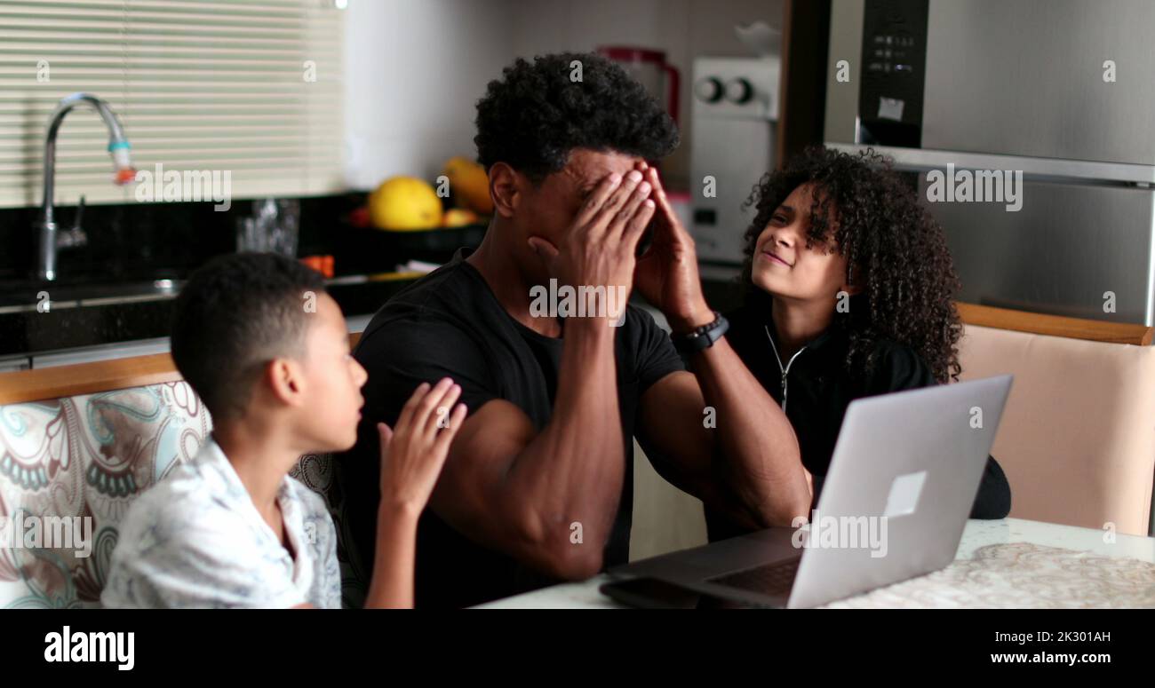 Black father working at home while children interrupt and complain ...