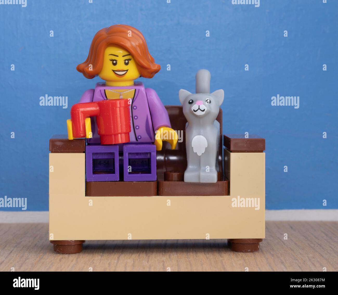 Lego woman sitting on a sofa with a gray cat and relaxing with a cup of ...