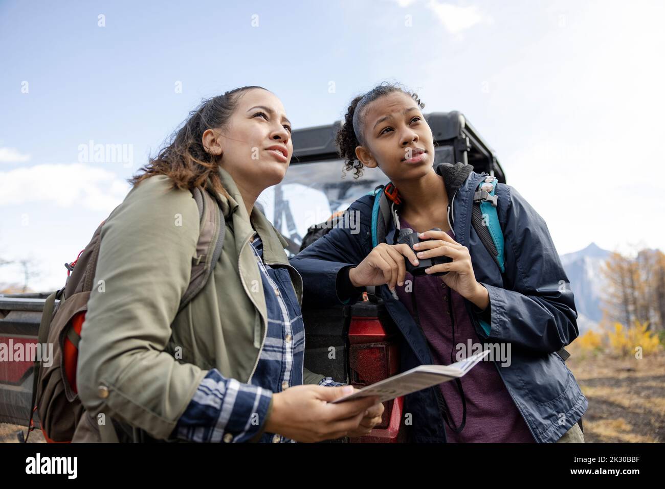 Mother and daughter with hiking trail map and binoculars looking away ...