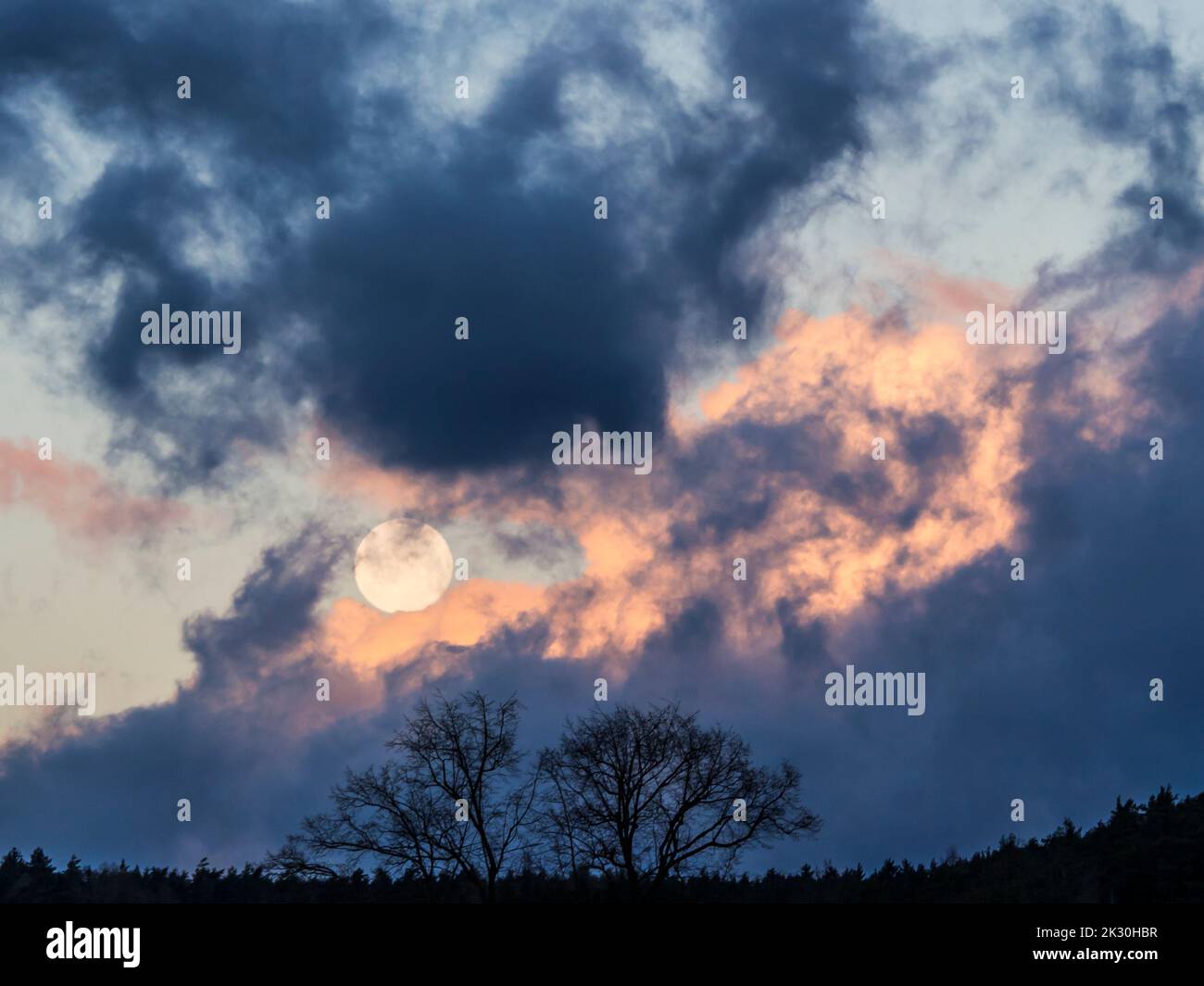 Full moon rising behind storm clouds Stock Photo - Alamy