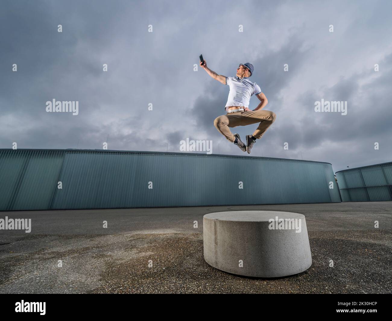 Young man jumping over concrete bench and taking selfie through mobile ...
