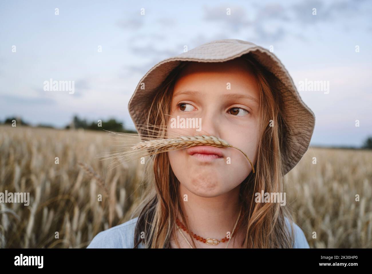 Cute girl in hat making mustache of rye corn at farm Stock Photo - Alamy